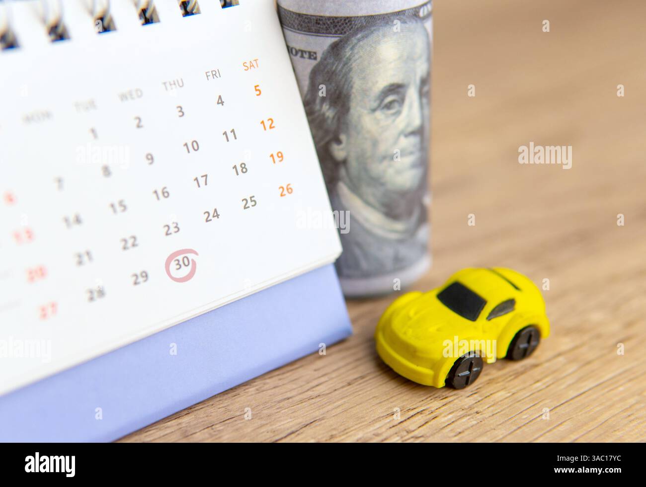 A calendar, rolled stack of US hundred dollar bills and a small toy car ...