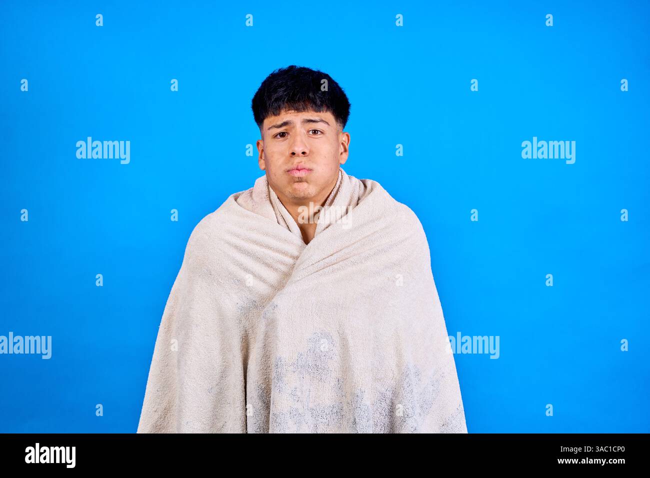 Sick man wrapped in towel shivering with cold on blue background ...