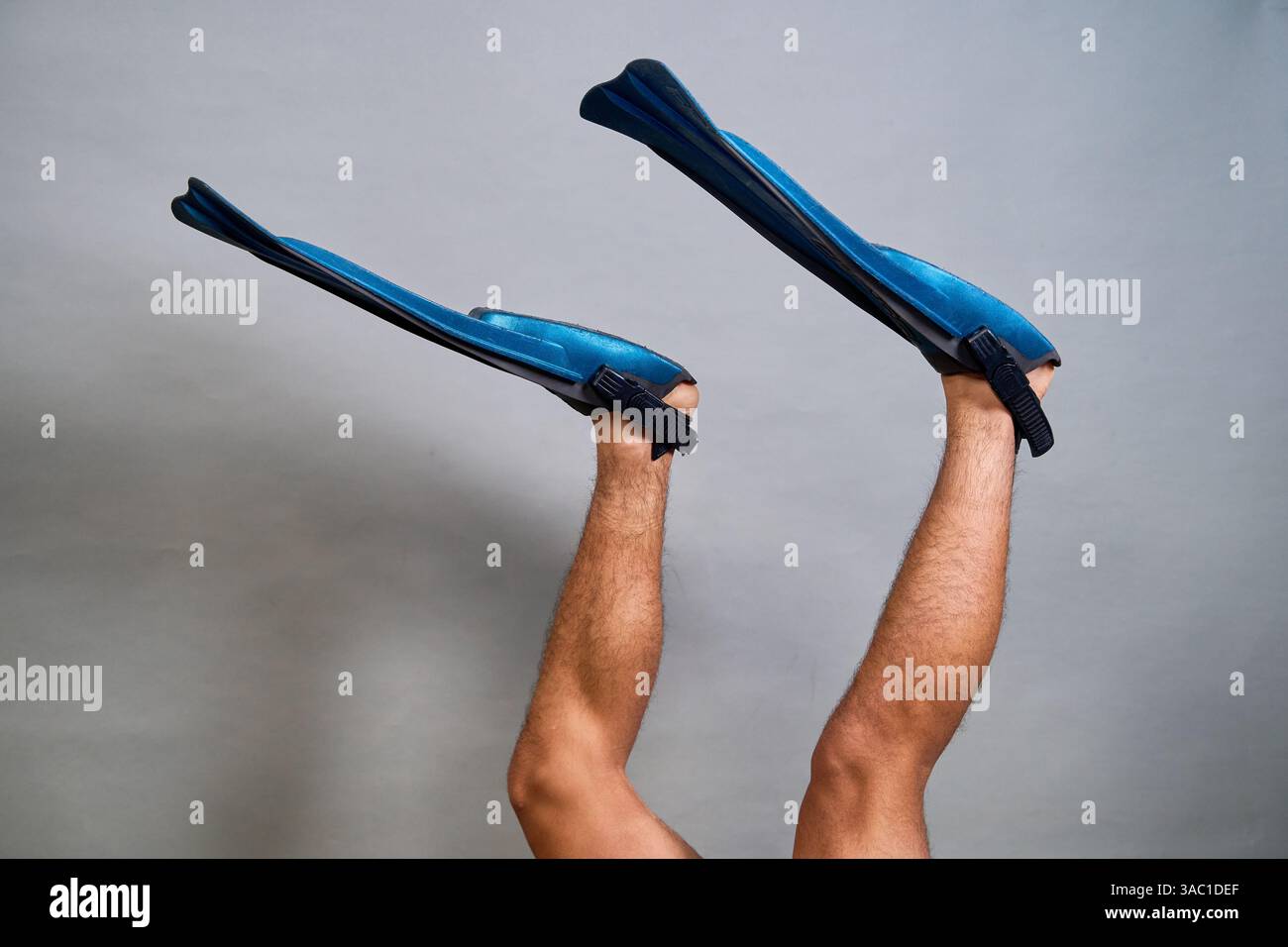 Hairy male legs wearing blue diving flippers lifted up against a gray ...
