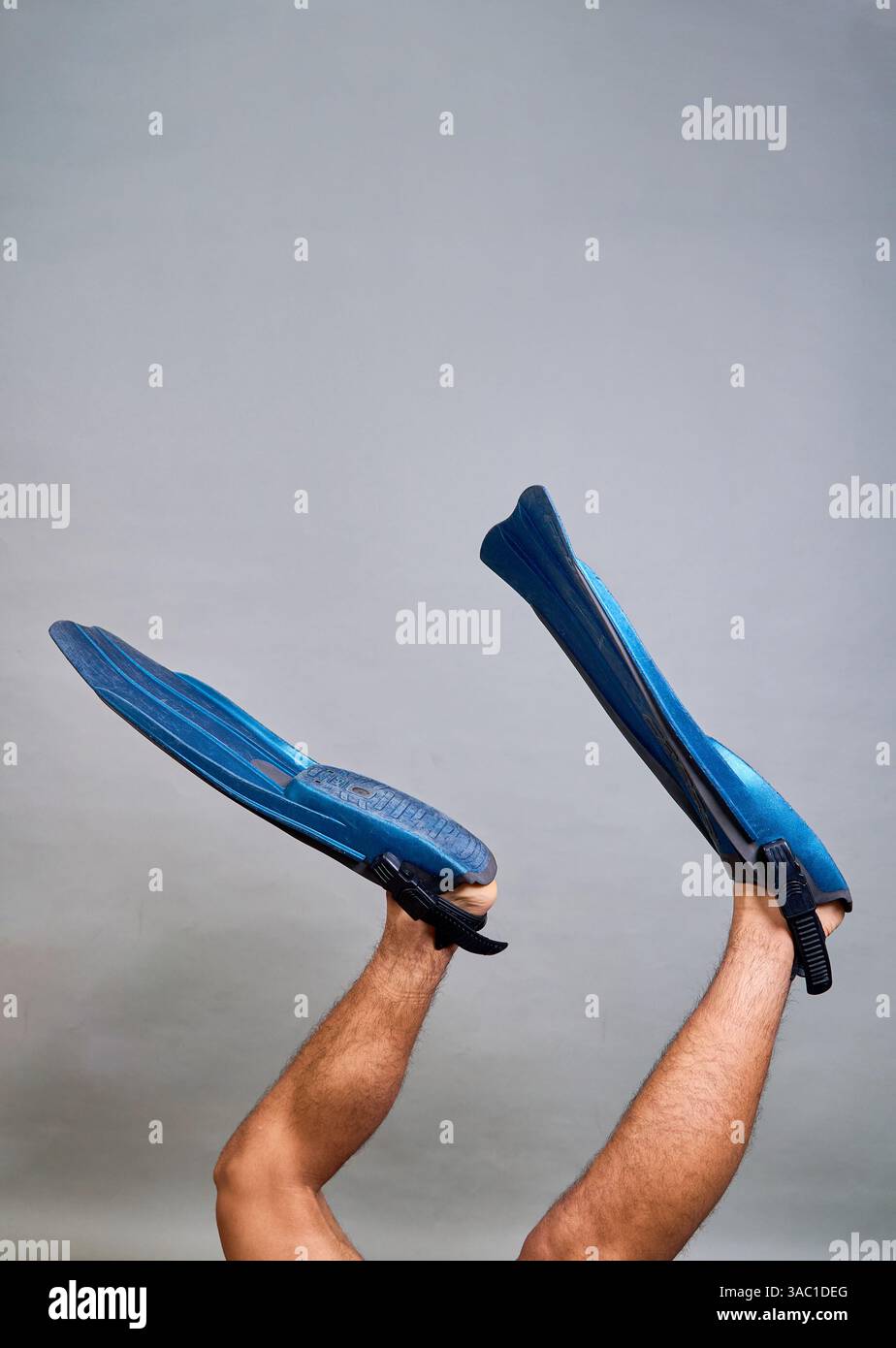 Diver wearing blue diving fins lifts legs up against a gray background ...