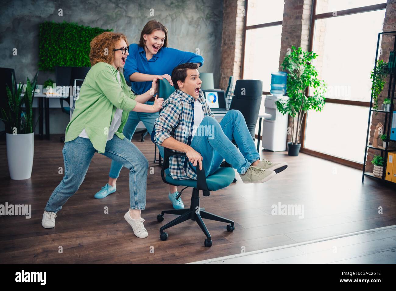 Group of colleagues having fun in the office rolling on a chair ...
