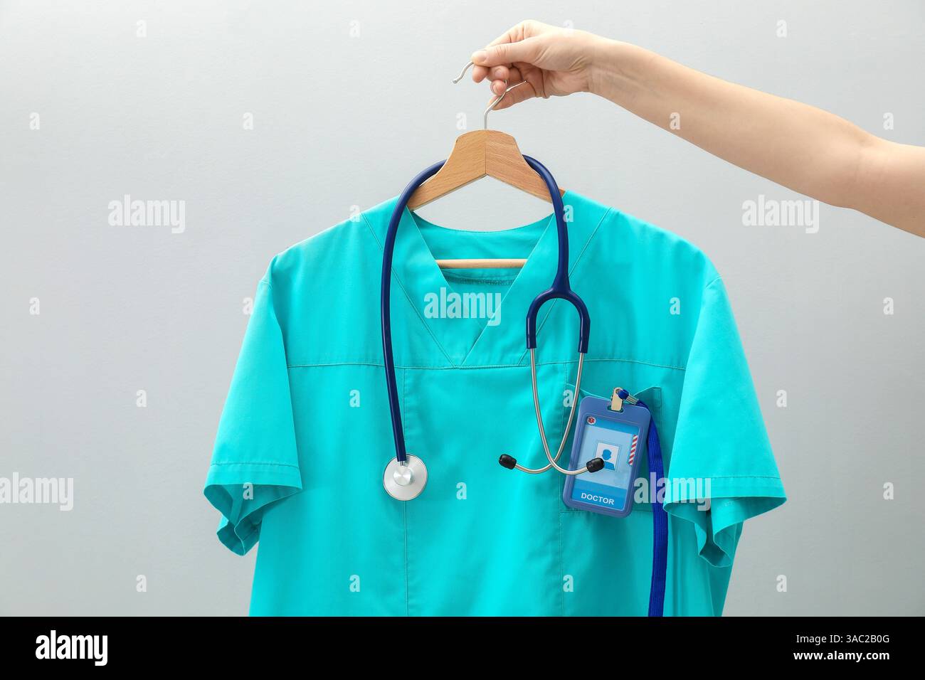 Woman holding hanger with medical worker uniform, stethoscope and badge ...