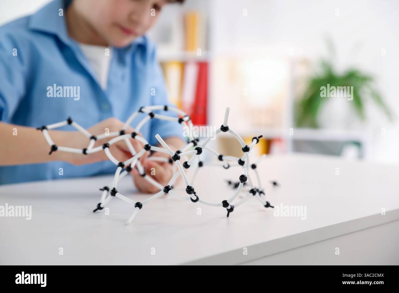 Boy making DNA structure model at desk indoors, closeup. Space for text ...