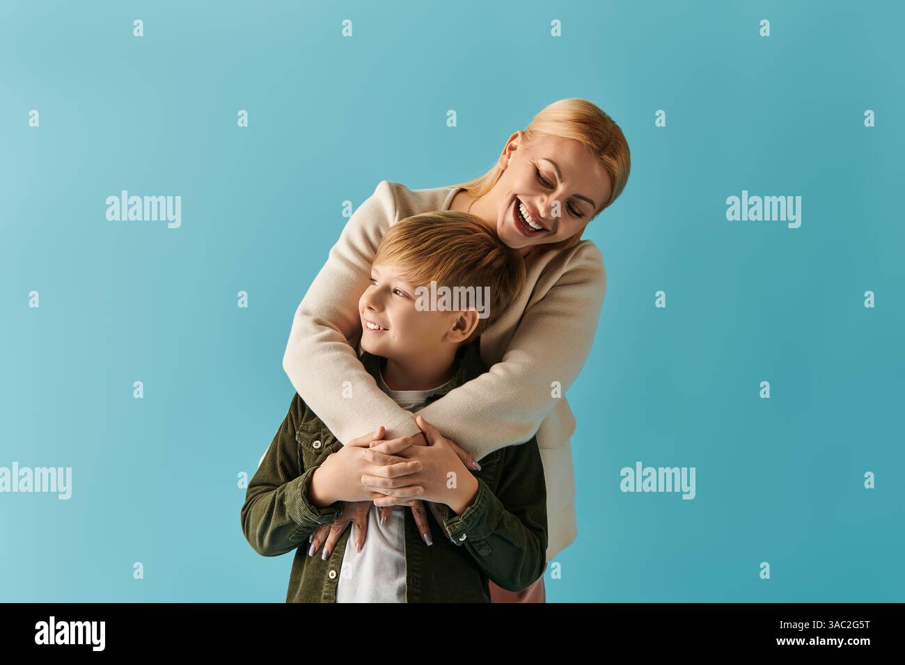 A joyful mother hugs her smiling son against a bright blue backdrop ...