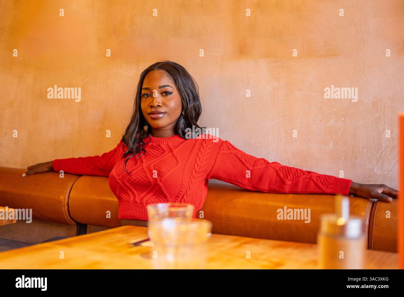 Confident young woman sitting in a restaurant booth, enjoying a moment ...