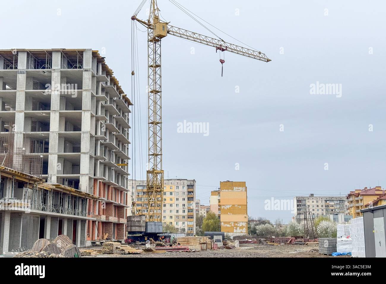A tall construction crane stands beside a partially built concrete ...