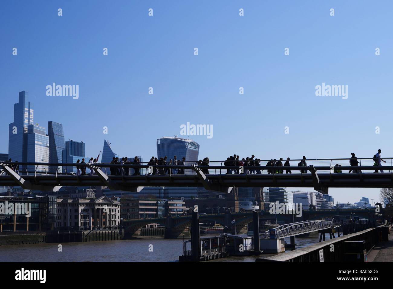 People walk over Millenium Bridge with The City of London buildings in ...