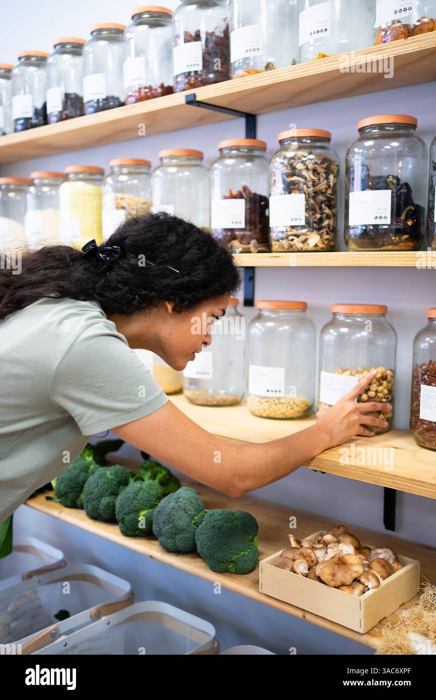 Young woman shopping for groceries in a zero-waste store, selecting ...