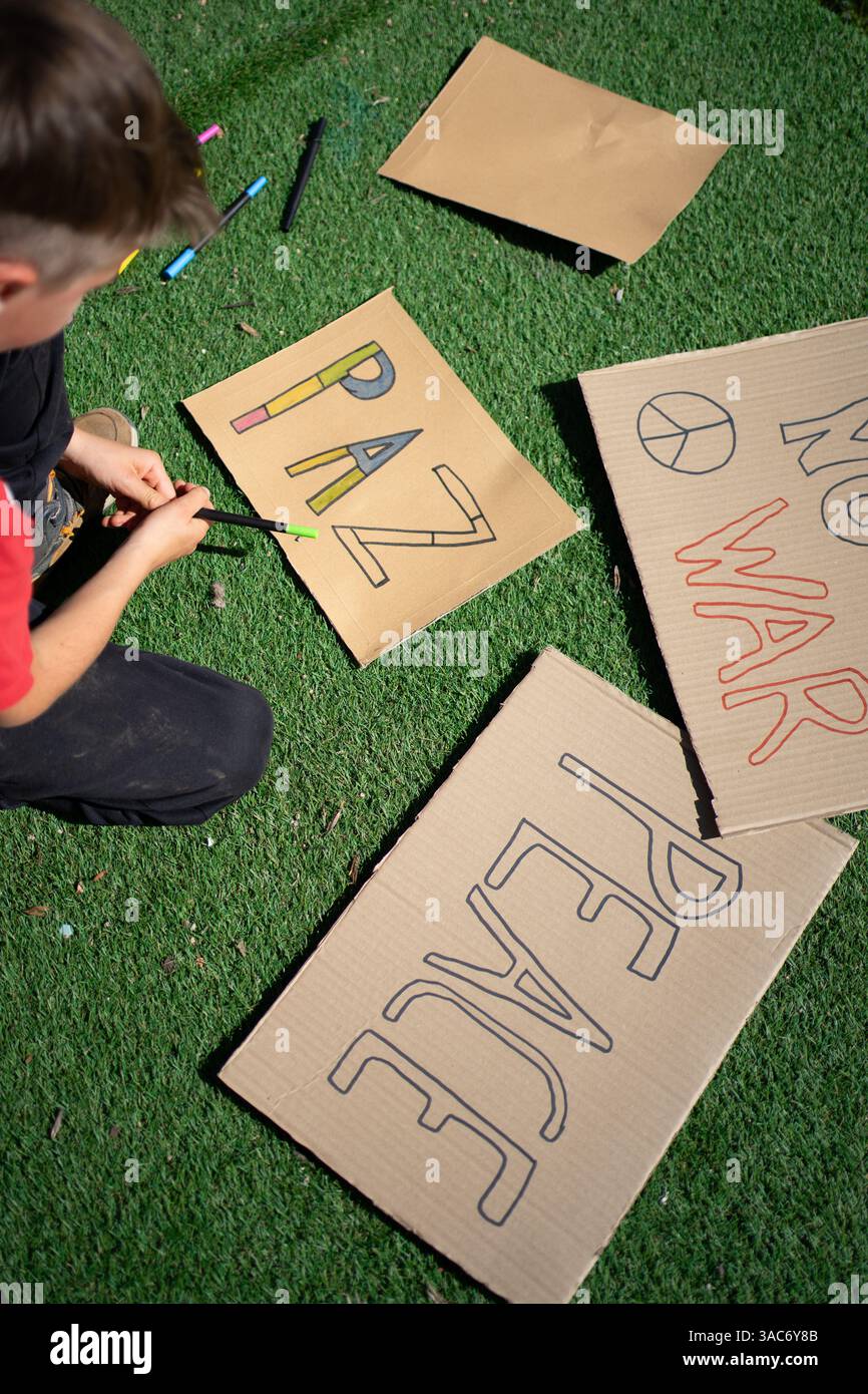 Caucasian boy drawing peace slogans on cardboard to create protest ...