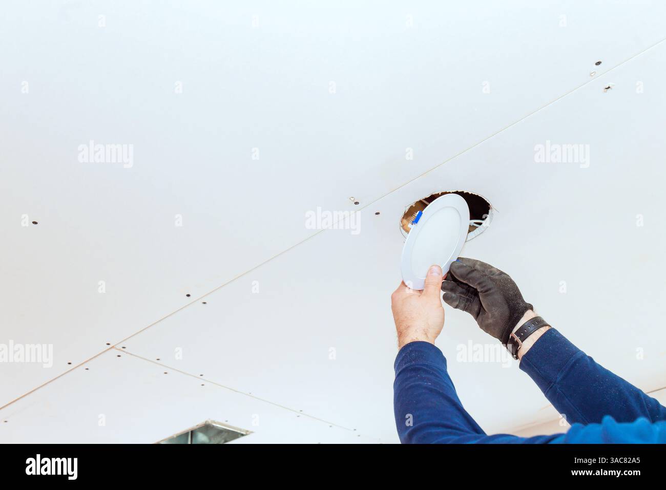 Electrician is fixing recessed light fixture in ceiling as home remodel ...