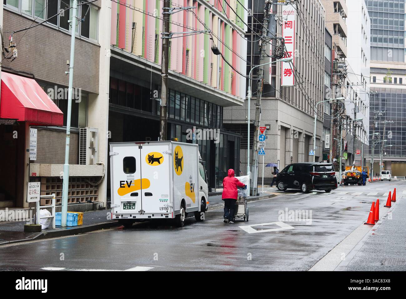 Street in Tokyo's Kayabacho area with old and new buildings and Yakult worker pushing a cart ...