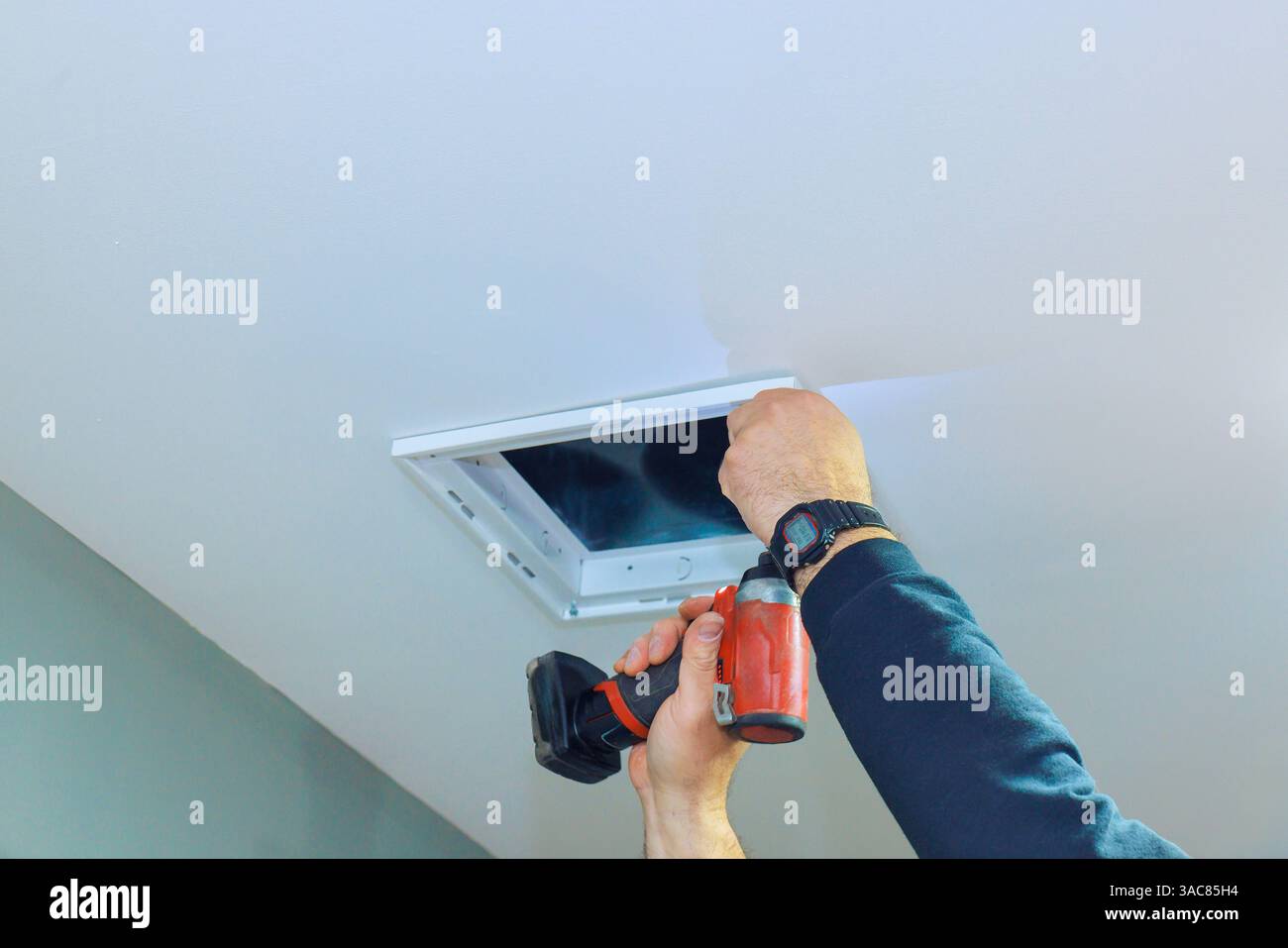 Handyman works on installing ventilation duct cover in ceiling of well ...