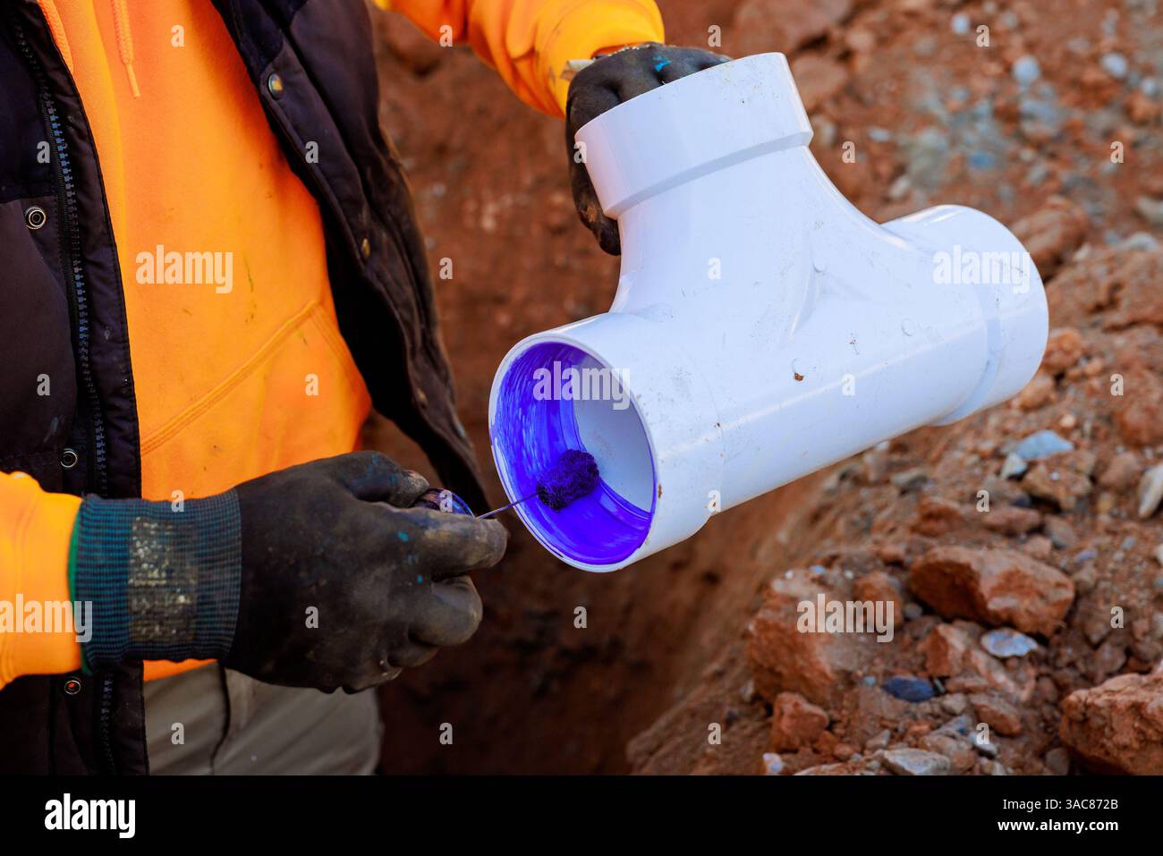 Construction worker is using adhesive on PVC pipe fitting at trench ...