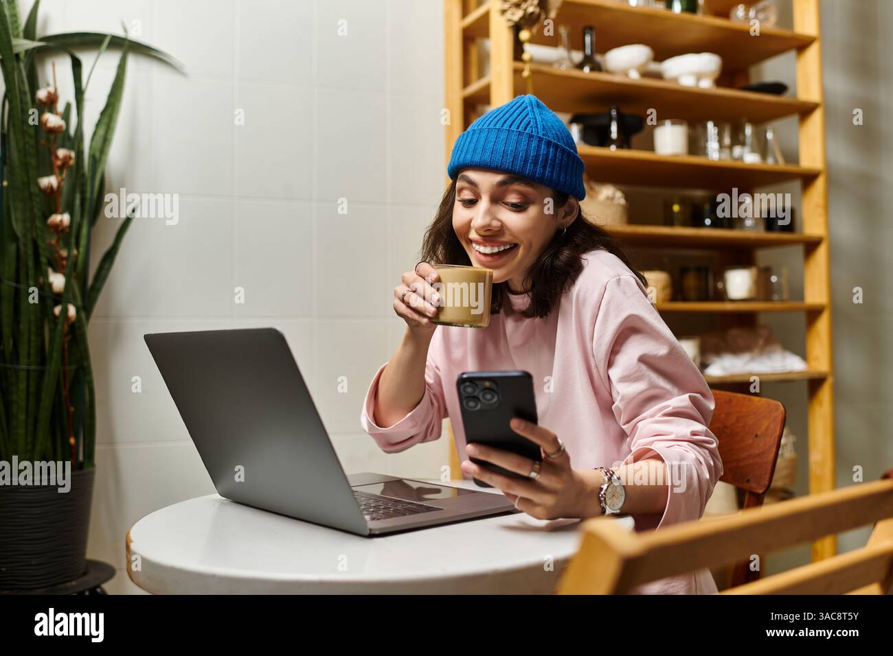 A young woman smiles while sipping coffee and working on her laptop in ...