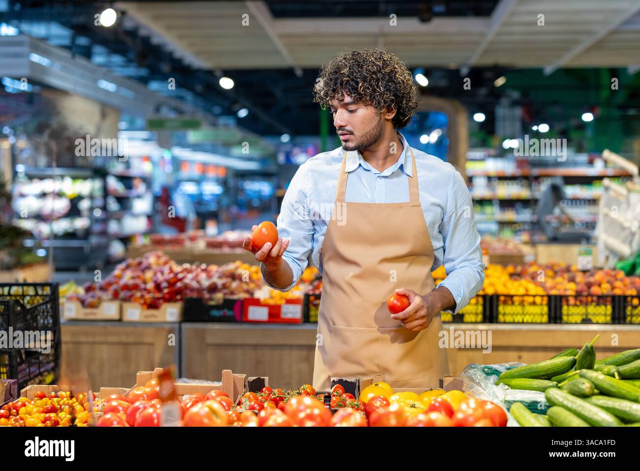 A shop assistant examines fresh tomatoes at a grocery store, surrounded ...