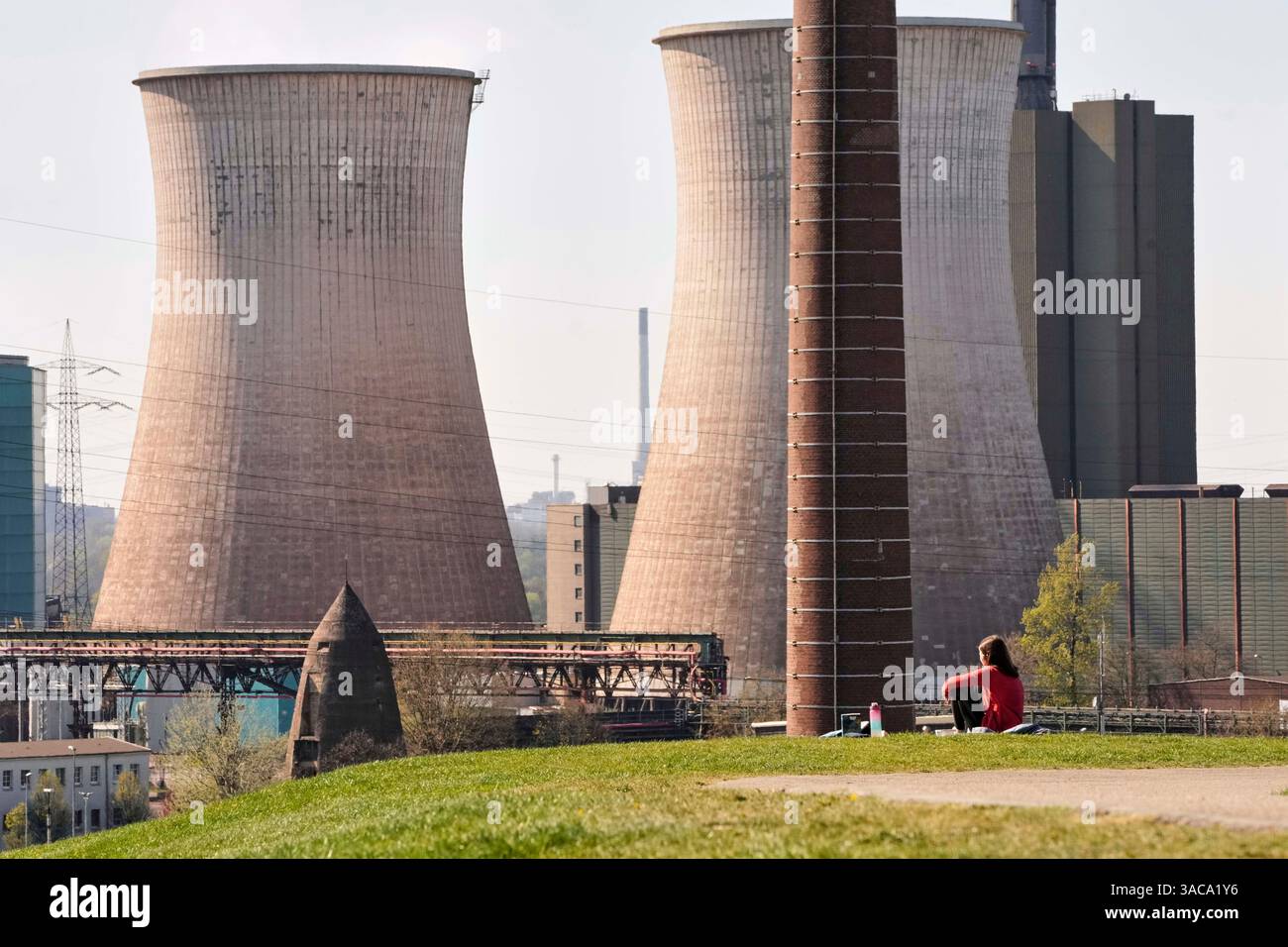 A young girl sits on the grass in front of a gas power station of the ...
