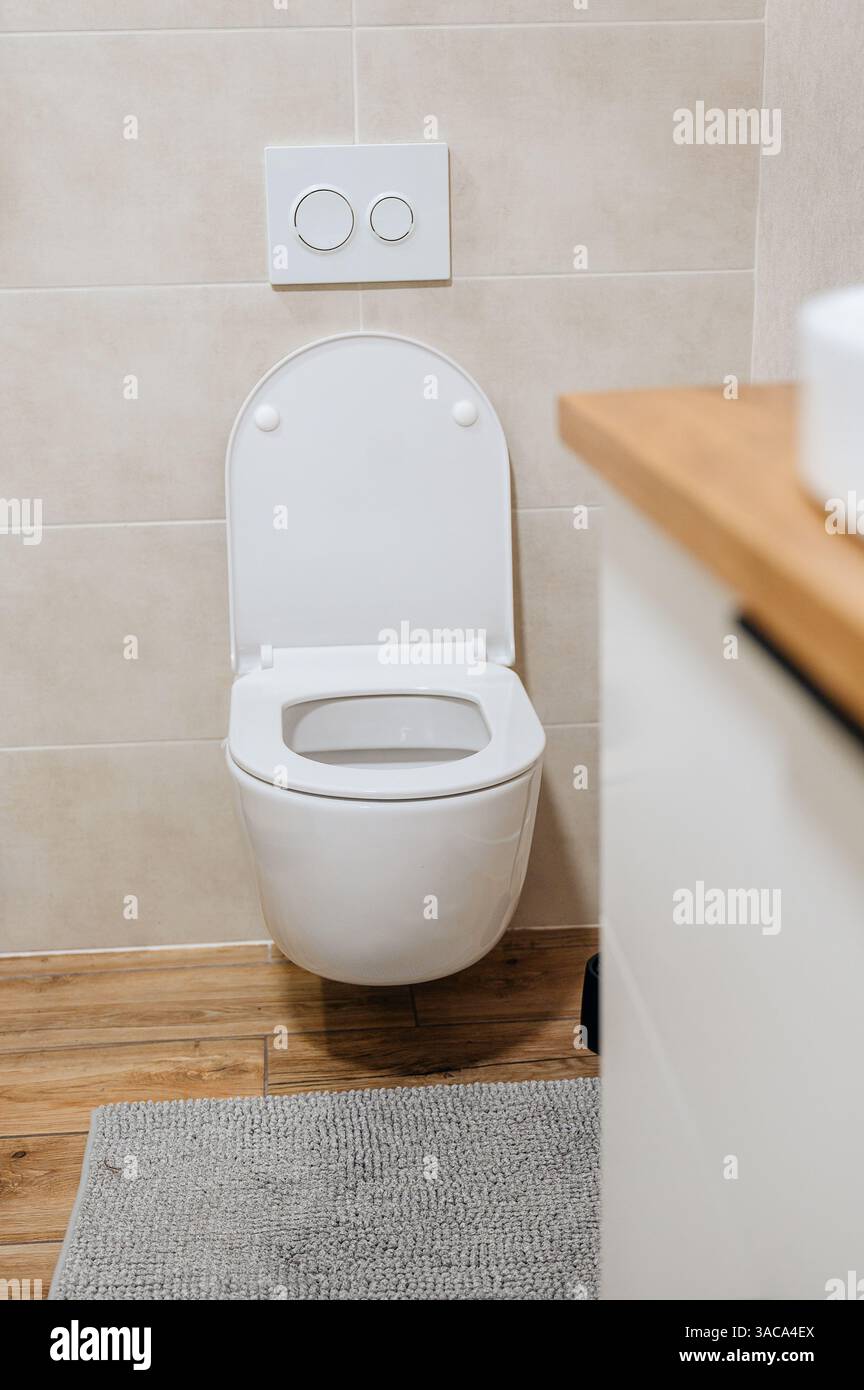 Toilet interior with wall hung toilet, white buttons and beige tiles ...