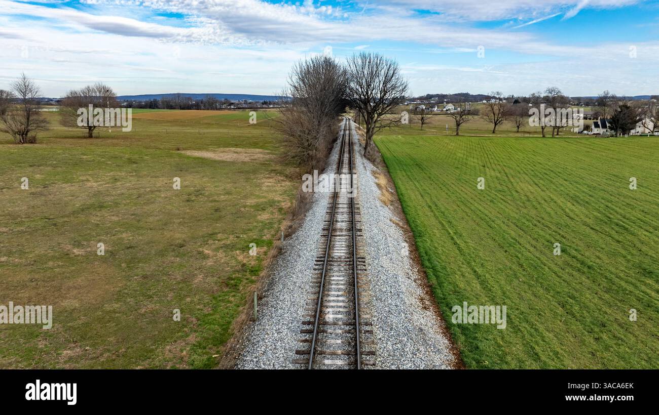 An expansive view showcases railway tracks running through open fields and distant hills in ...