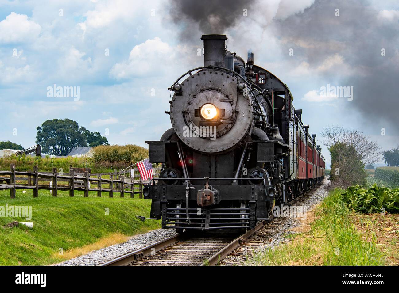 A historic steam locomotive travels along rural tracks, surrounded by ...