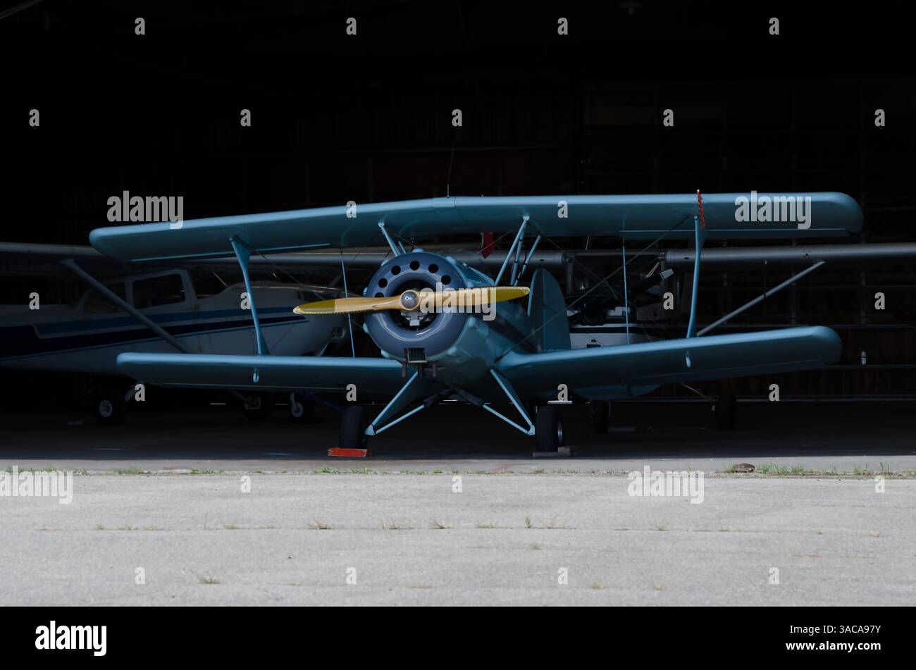 front view of vintage blue bi-plane parked at the entrance to a hangar ...