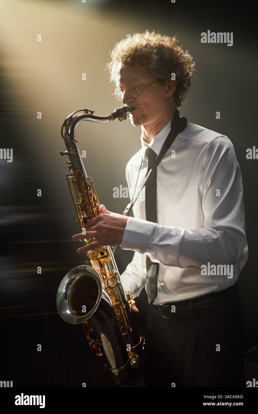 Vertical shot of adult male saxophonist dressed in white shirt and ...