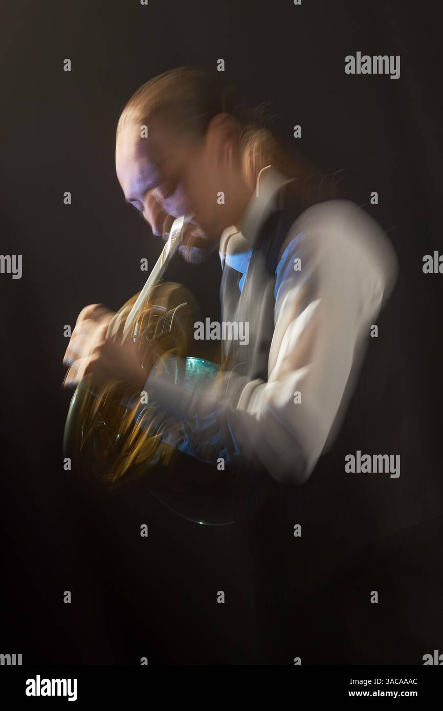 Vertical motion blur shot of professional male hornist playing French ...