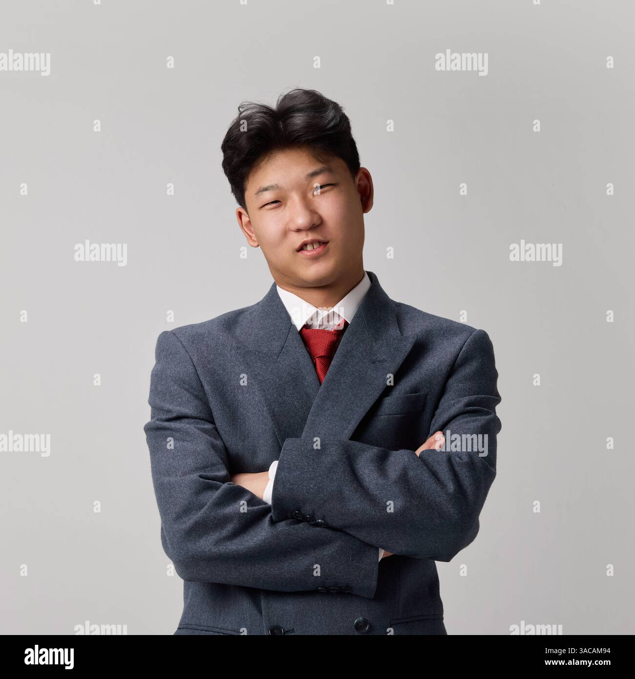 Close-up of smiling young man in formal grey suit, posing with arms ...