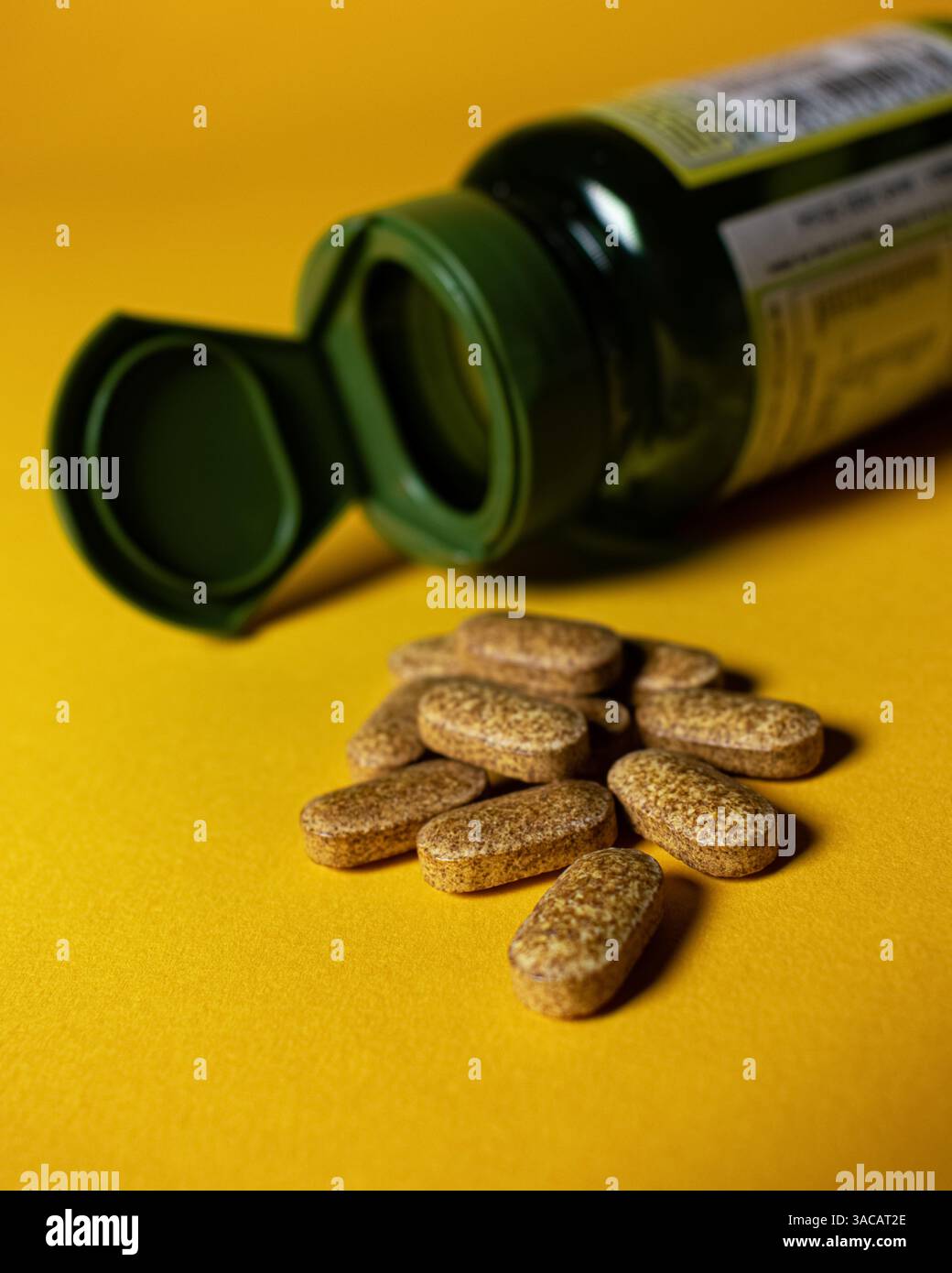 An open bottle of multivitamin tablets, pills on yellow background ...