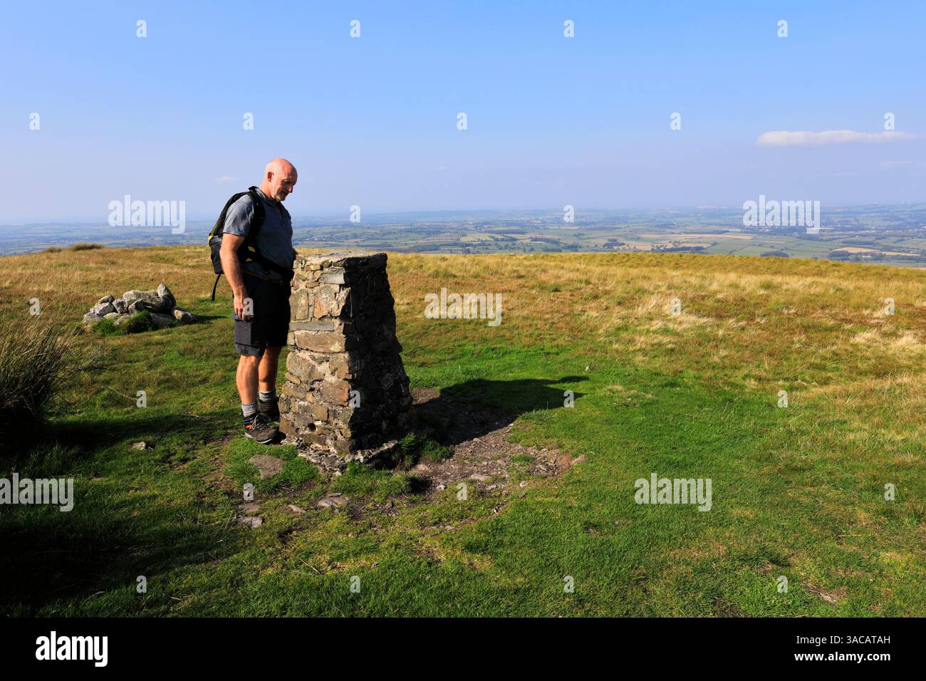 Walker at the summit cairn and OS Trig point, of Fellbarrow fell above ...