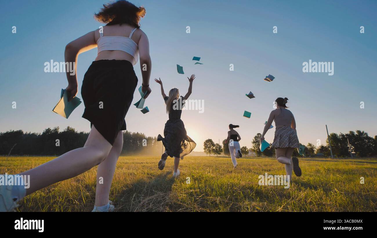 Group of high school students running in field throwing books ...