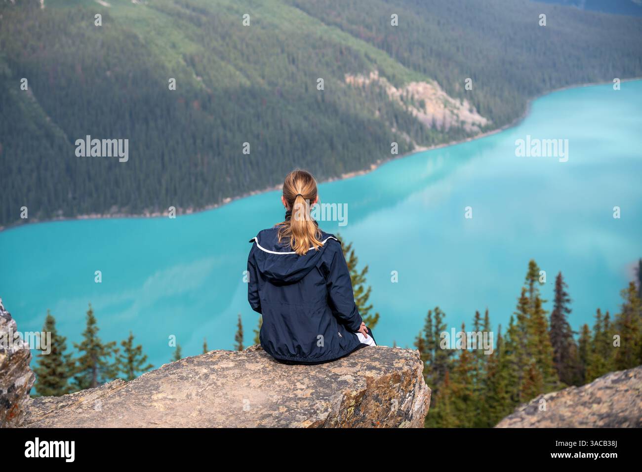 Tourist sitting on a rock ledge overlooking Peyto Lake in Banff ...
