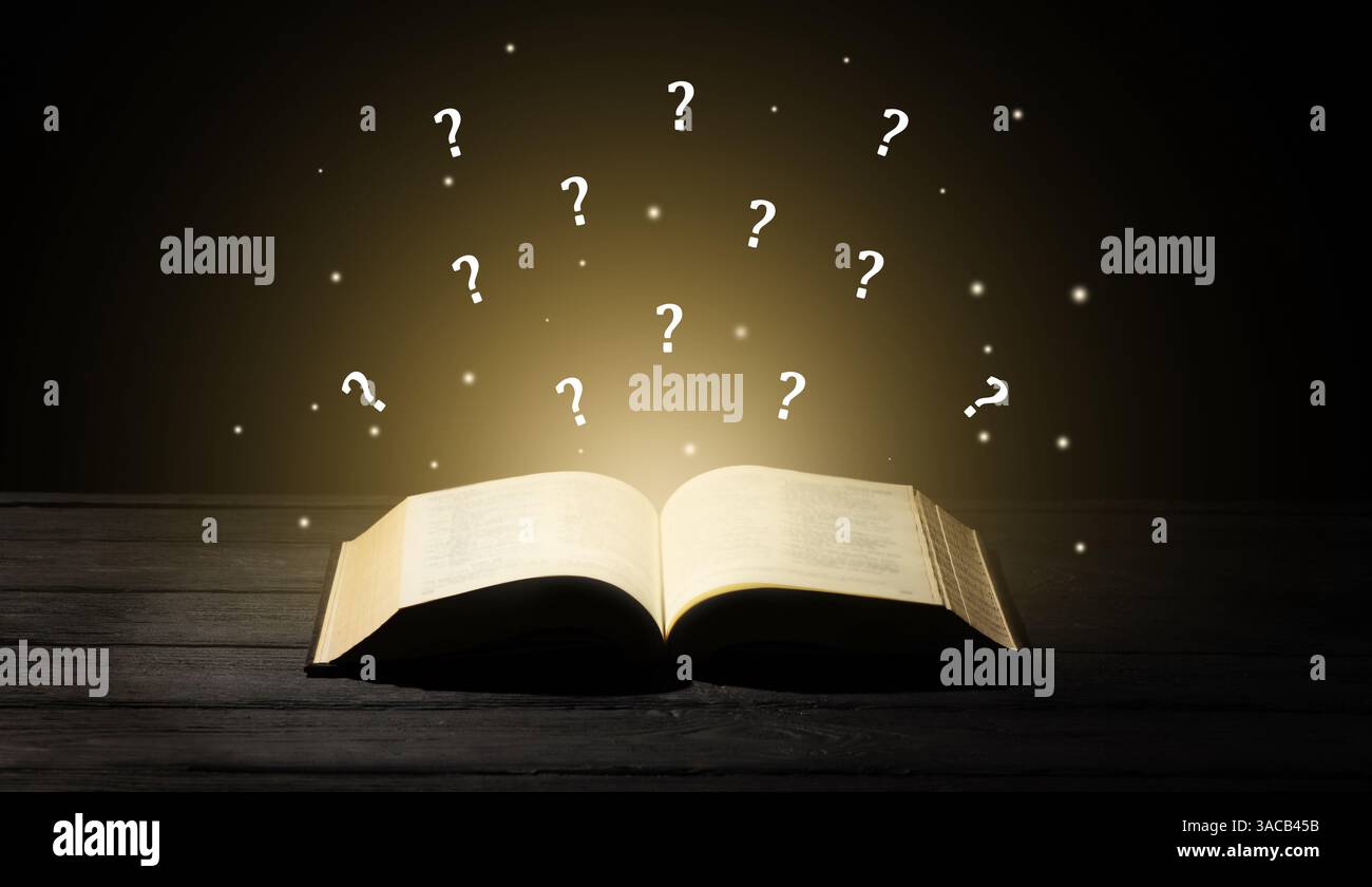 Glowing book with question marks over pages on wooden table against ...