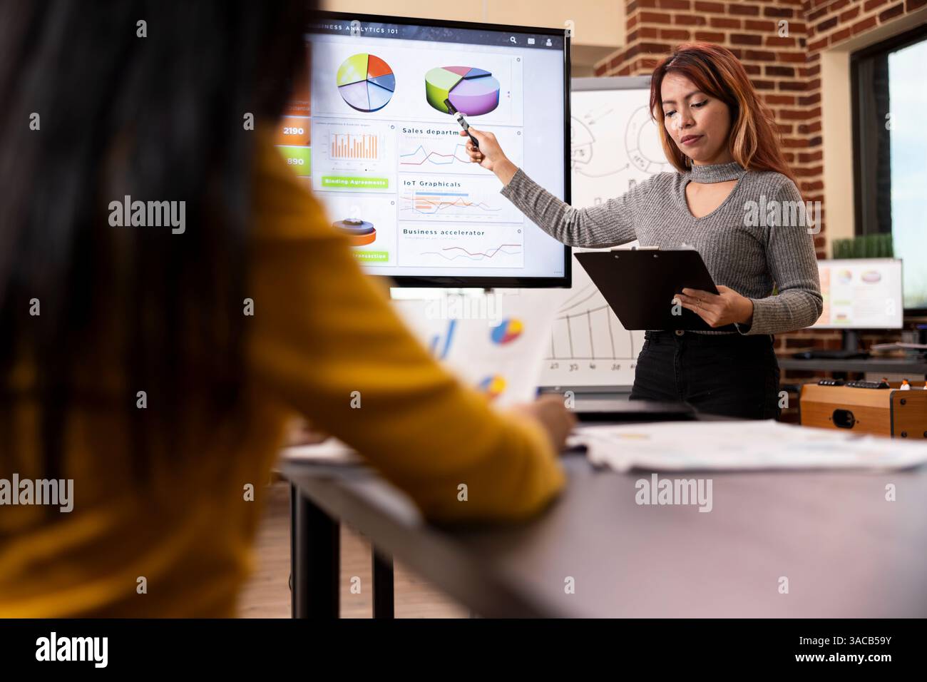 Asian businesswoman reading a document as she points towards the data analytics chart on digital ...