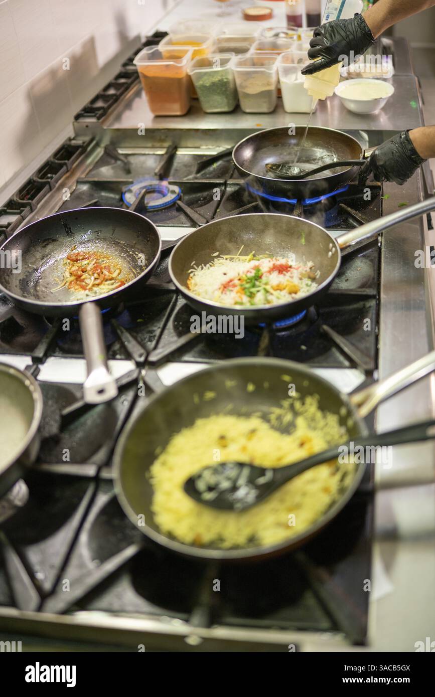 Chefs are pouring ingredients into pans on a professional gas stove ...