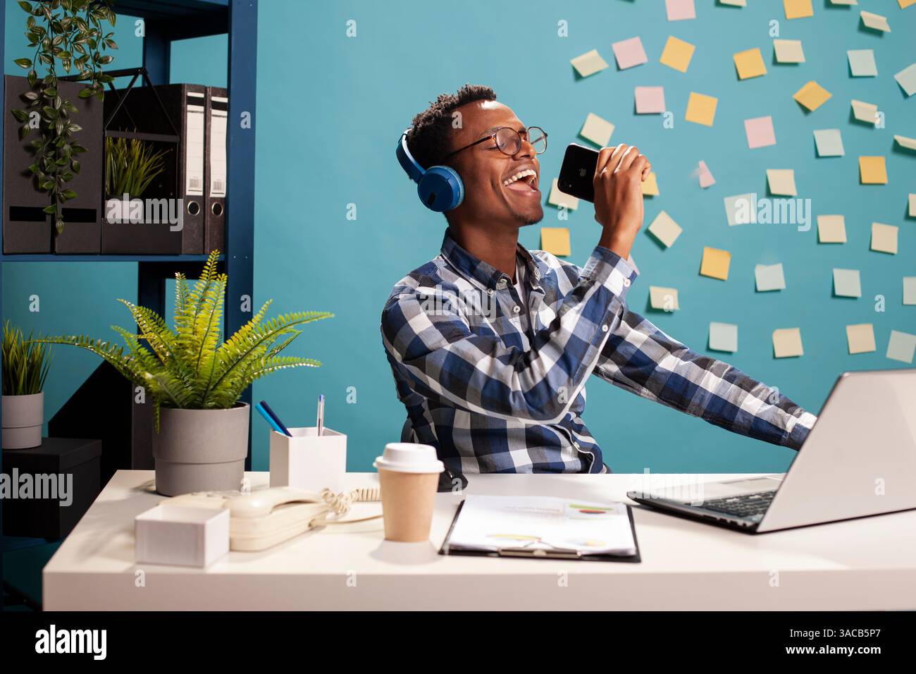 Male office worker enjoying karaoke at his desk, smiling and listening ...