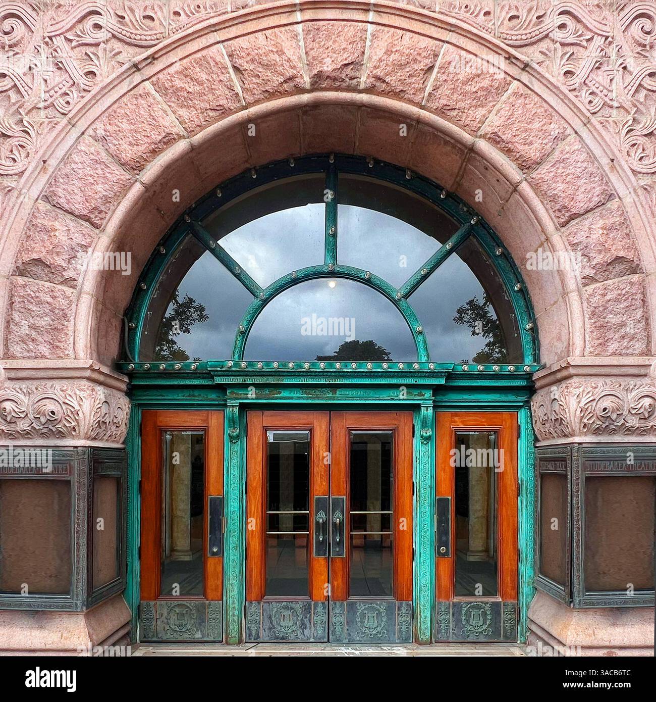 A richly detailed arched stone entrance with green metal framing and ...