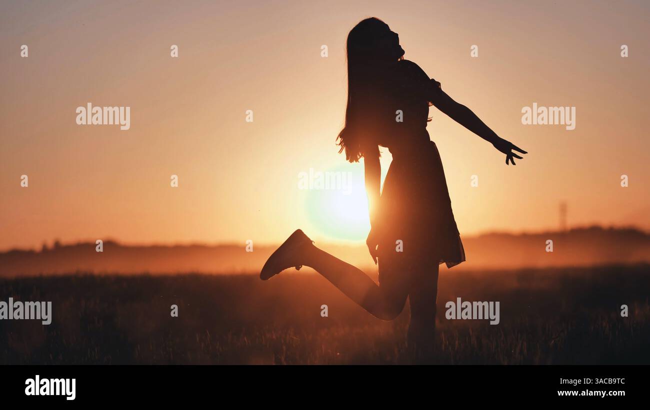 Silhouetted woman dancing freely in golden sunset field, embodying ...