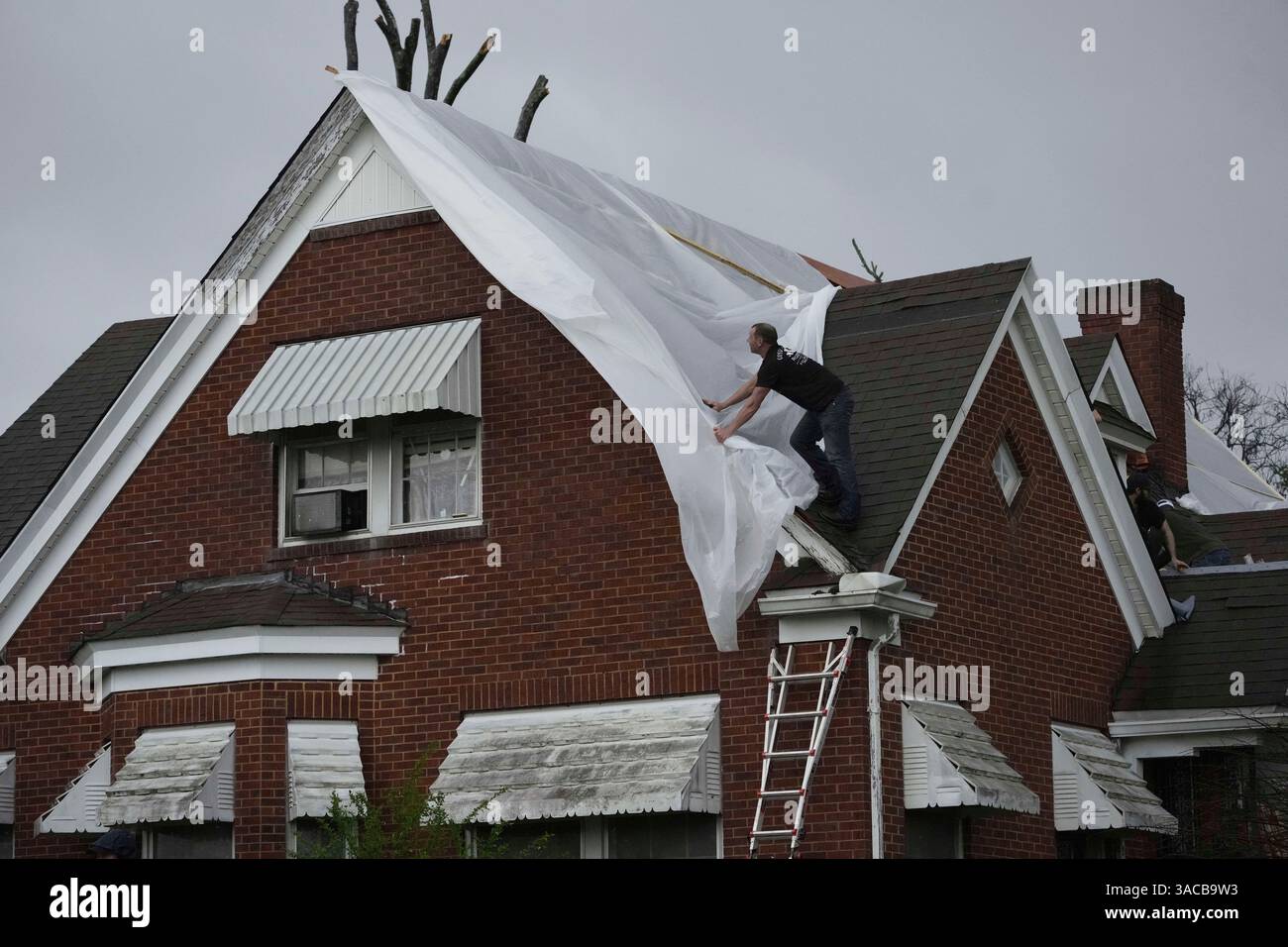 Jeremiah Coyle works to cover a roof in the rain following severe ...