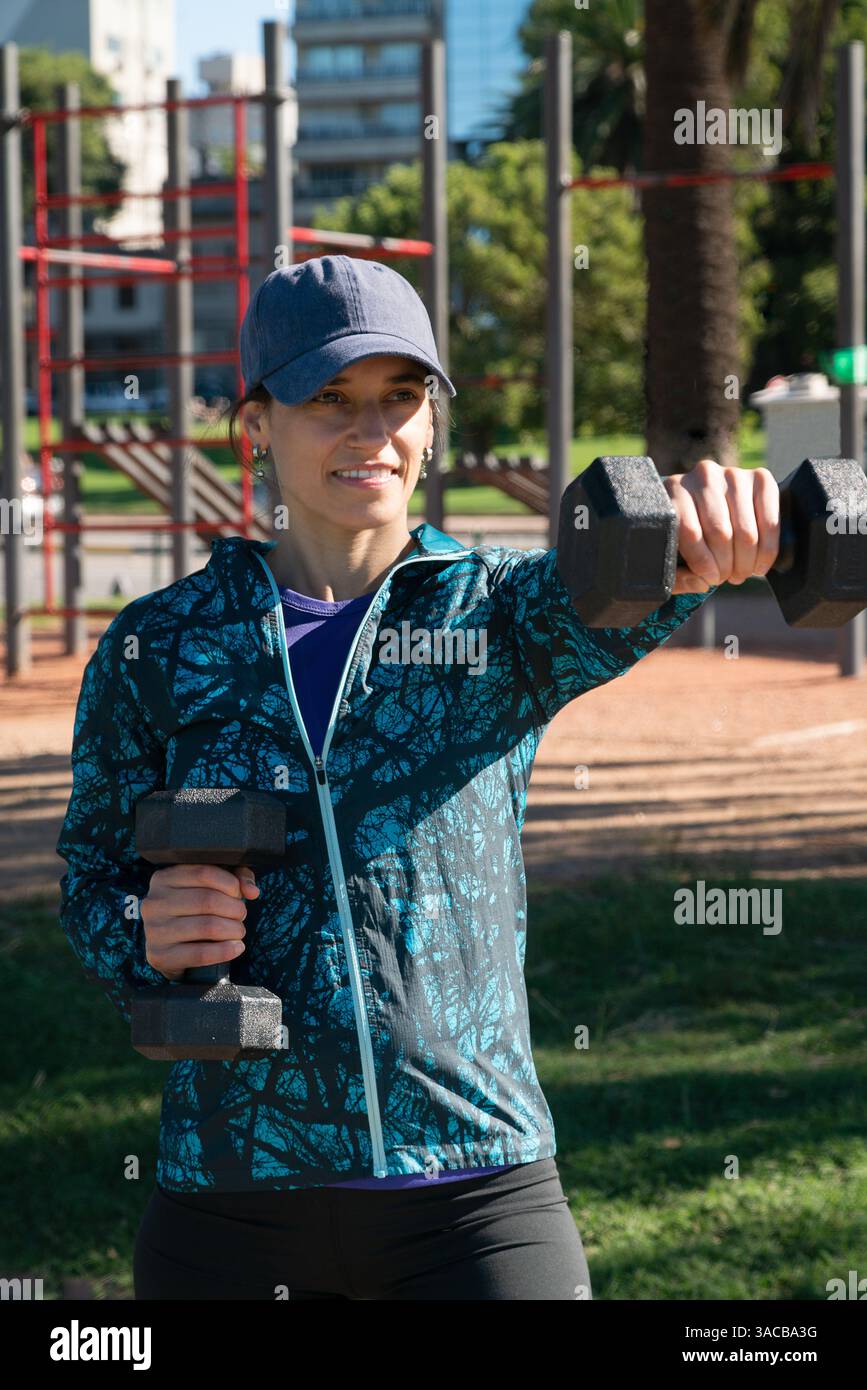 Fitness woman lifting weights outdoors in a park. Vertical frame Stock ...