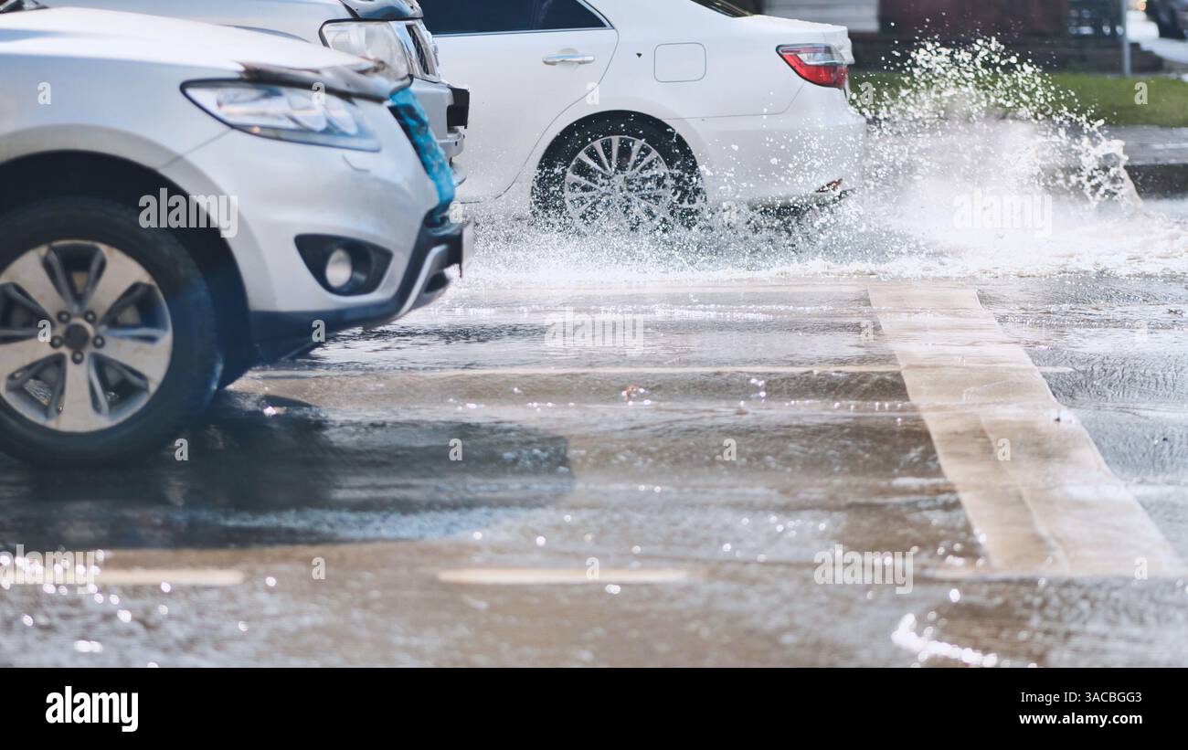 Splashing white vehicle sending water spray across urban roadway during ...