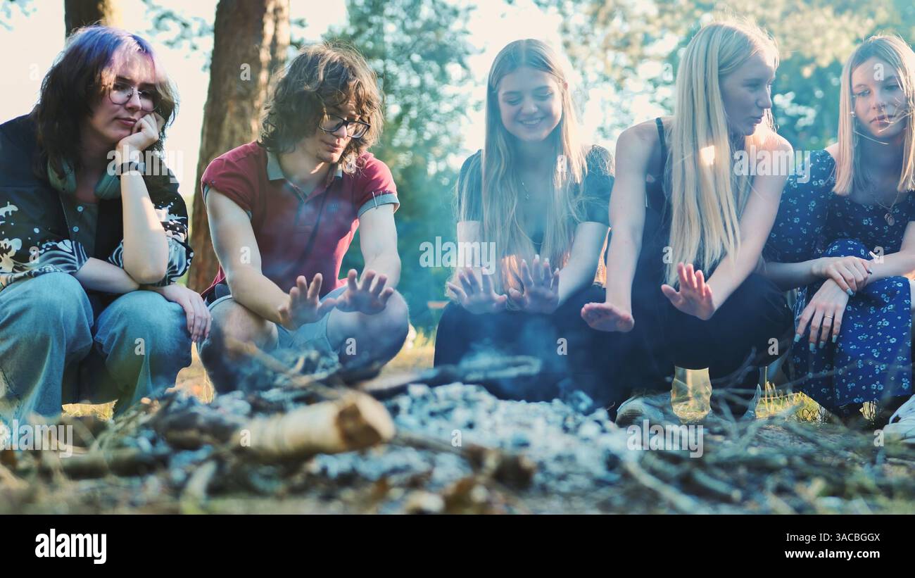 Group of young students warming their hands by a bonfire in a forest ...