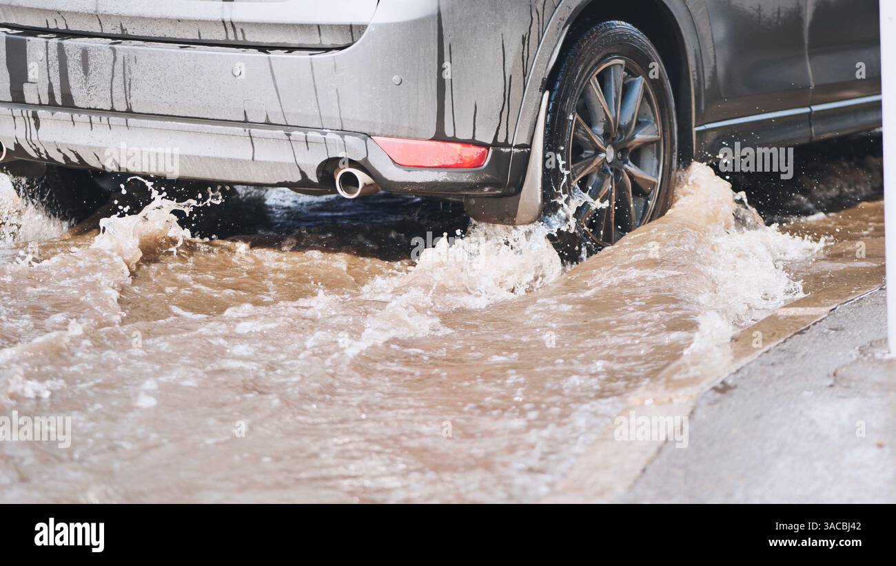 Muddy vehicle splashing through roadside puddle during wet, overcast ...