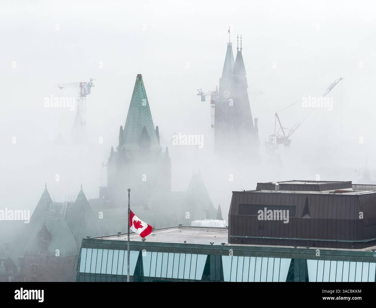 Foggy morning at Parliament Hill, Ottawa, with Canadian flag and cranes ...
