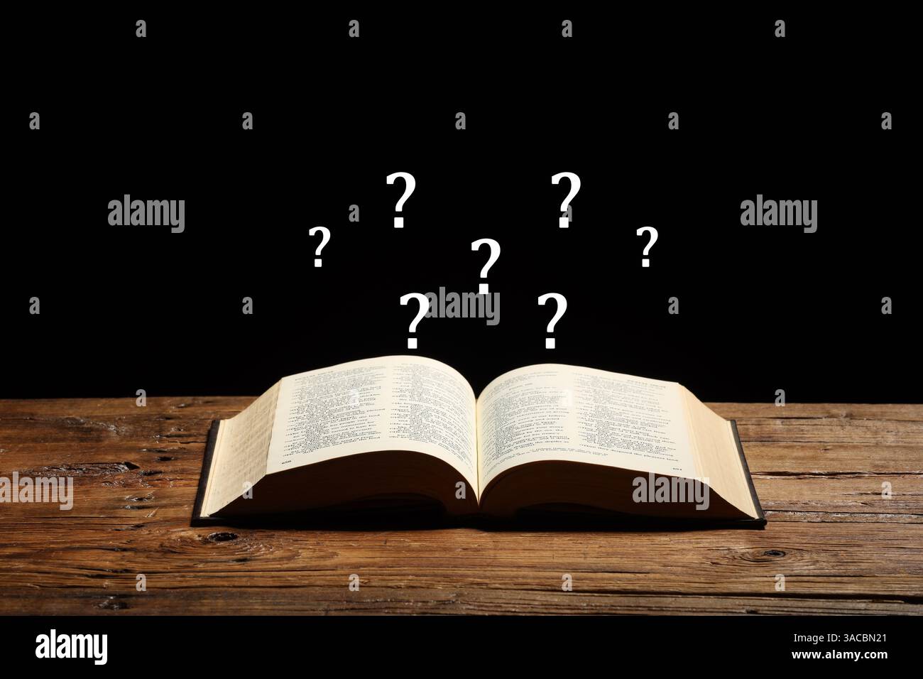 Question marks over open book on wooden table against black background ...