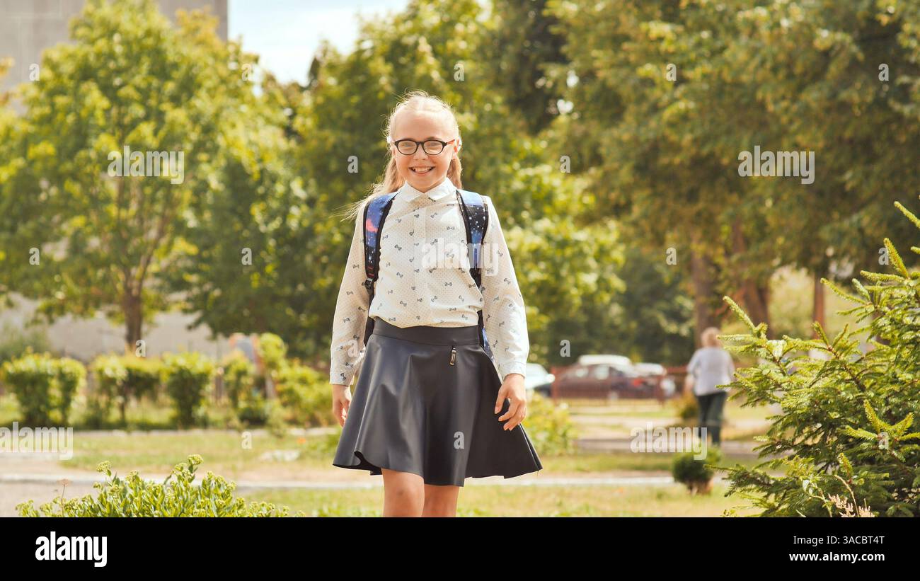 Cheerful schoolgirl with glasses walking through sunny park, backpack ...