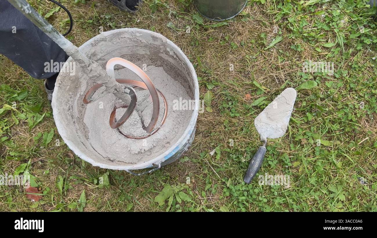 Construction worker mixing cement in bucket using mixing paddle and ...