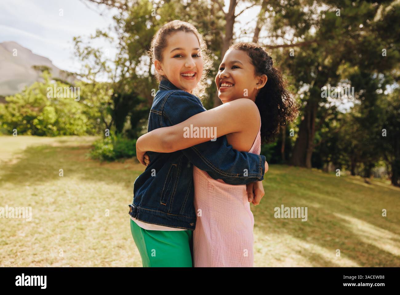Two happy friends hug cheerfully in a lush green park under a sunny sky ...