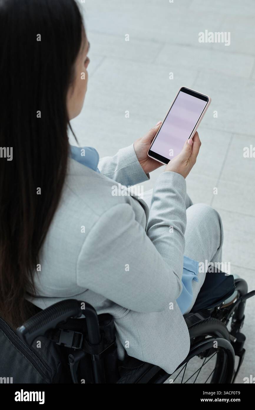 Vertical portrait of young woman in wheelchair holding smartphone with ...