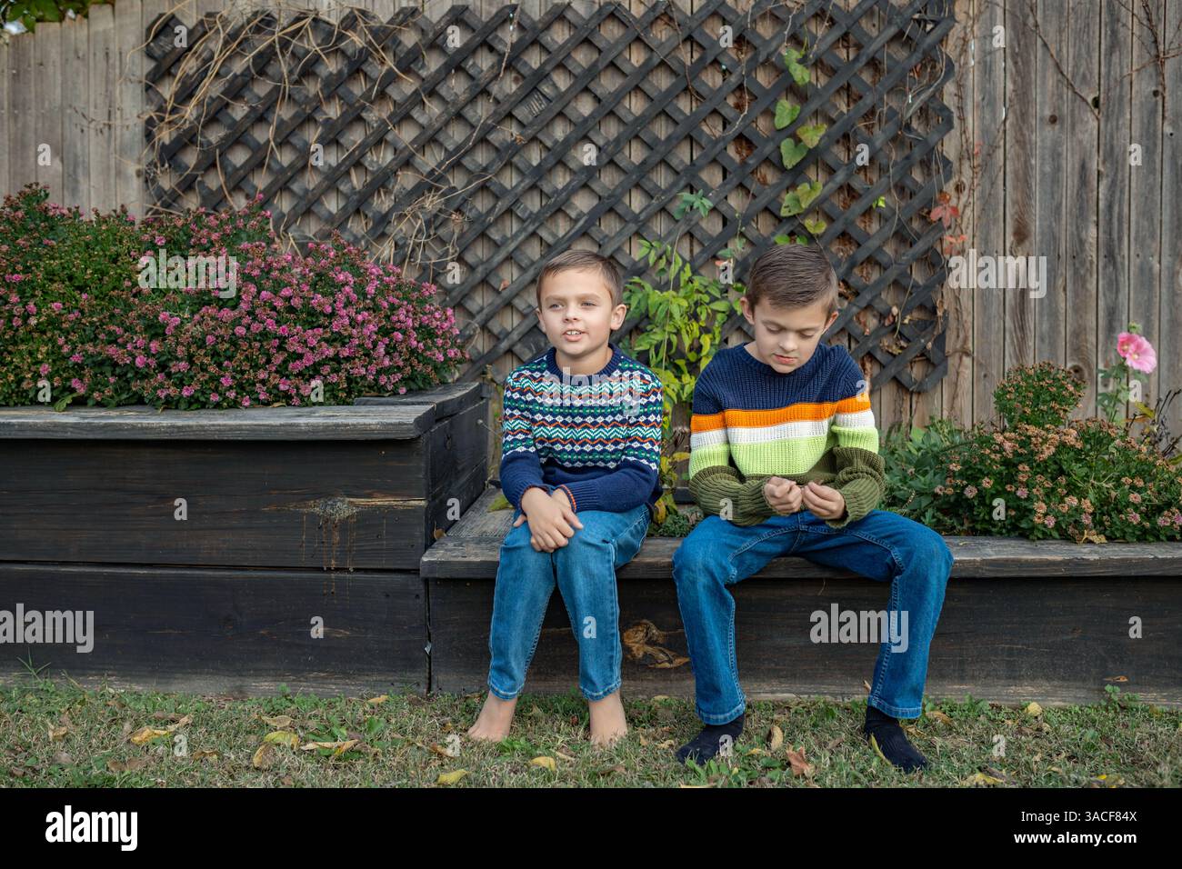 Two boys sitting on a bench near flowers and a wooden lattice fence ...