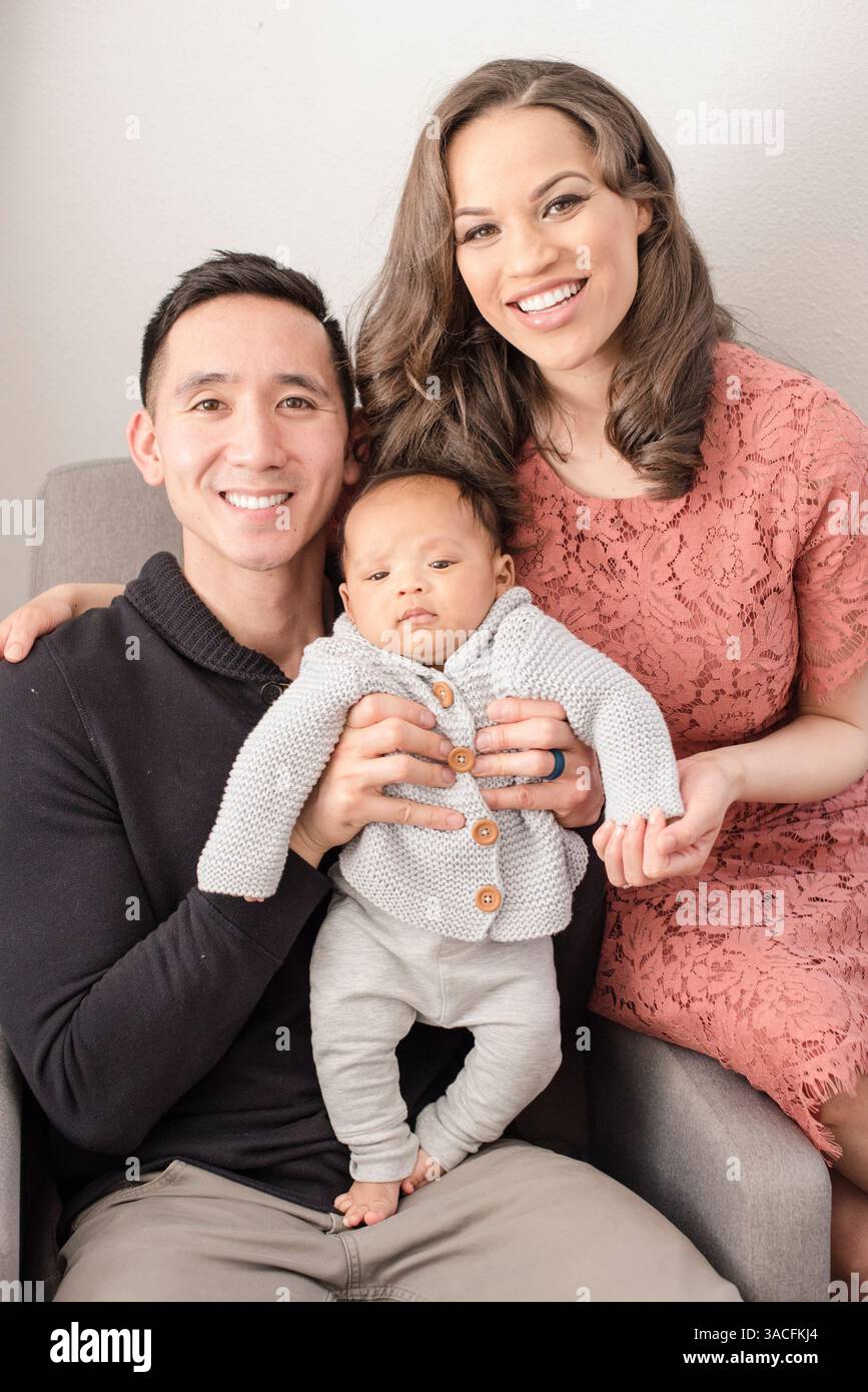 Smiling parents pose with baby sitting between them on a chair Stock ...